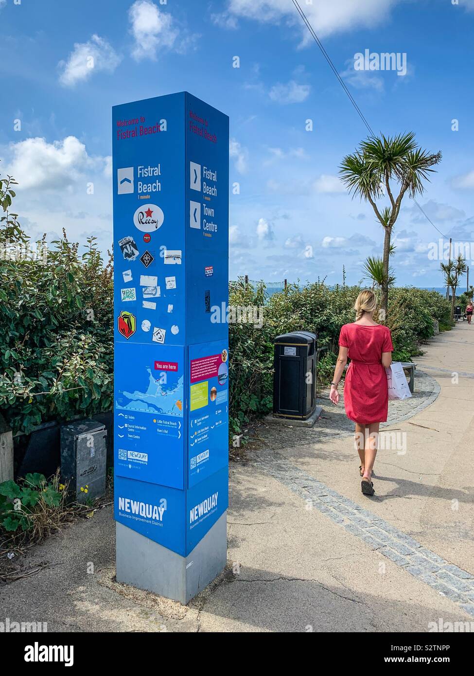 Woman in red dress walking past sign for fistral beach in Newquay ...