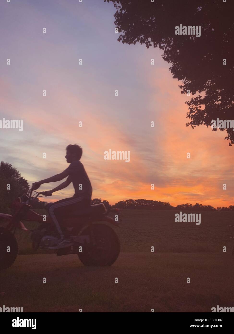 Boy riding motorcycle in the countryside with sunset behind him Stock ...
