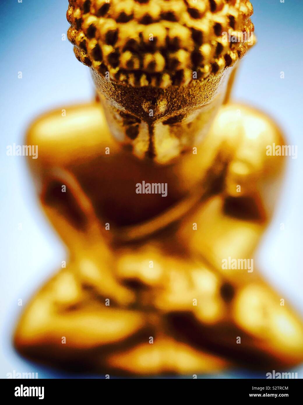 Macro photo of a golden tiny Buddha statue against a grey background ...