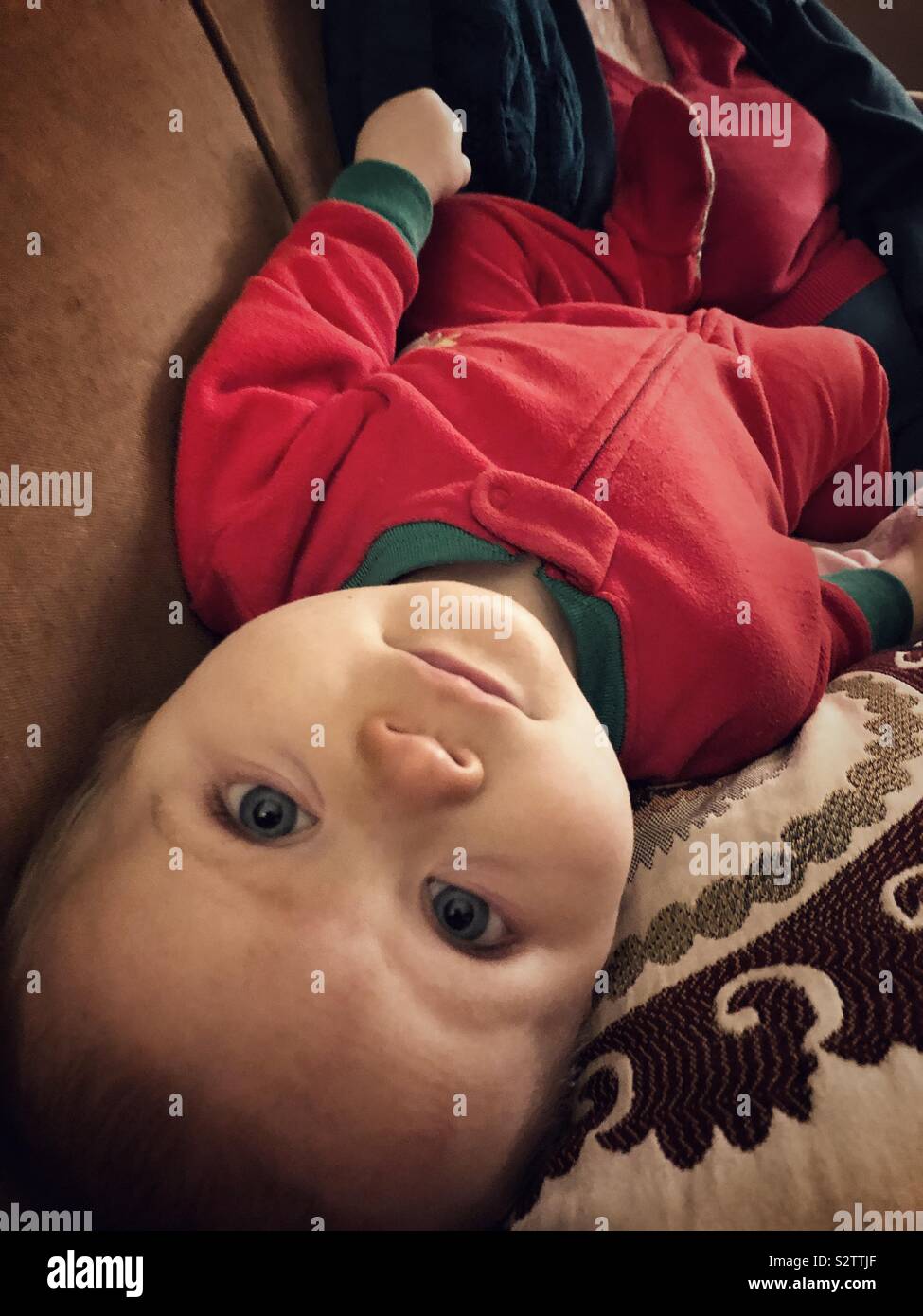 A baby lying upside-down staring at the camera. The baby is wearing a ...