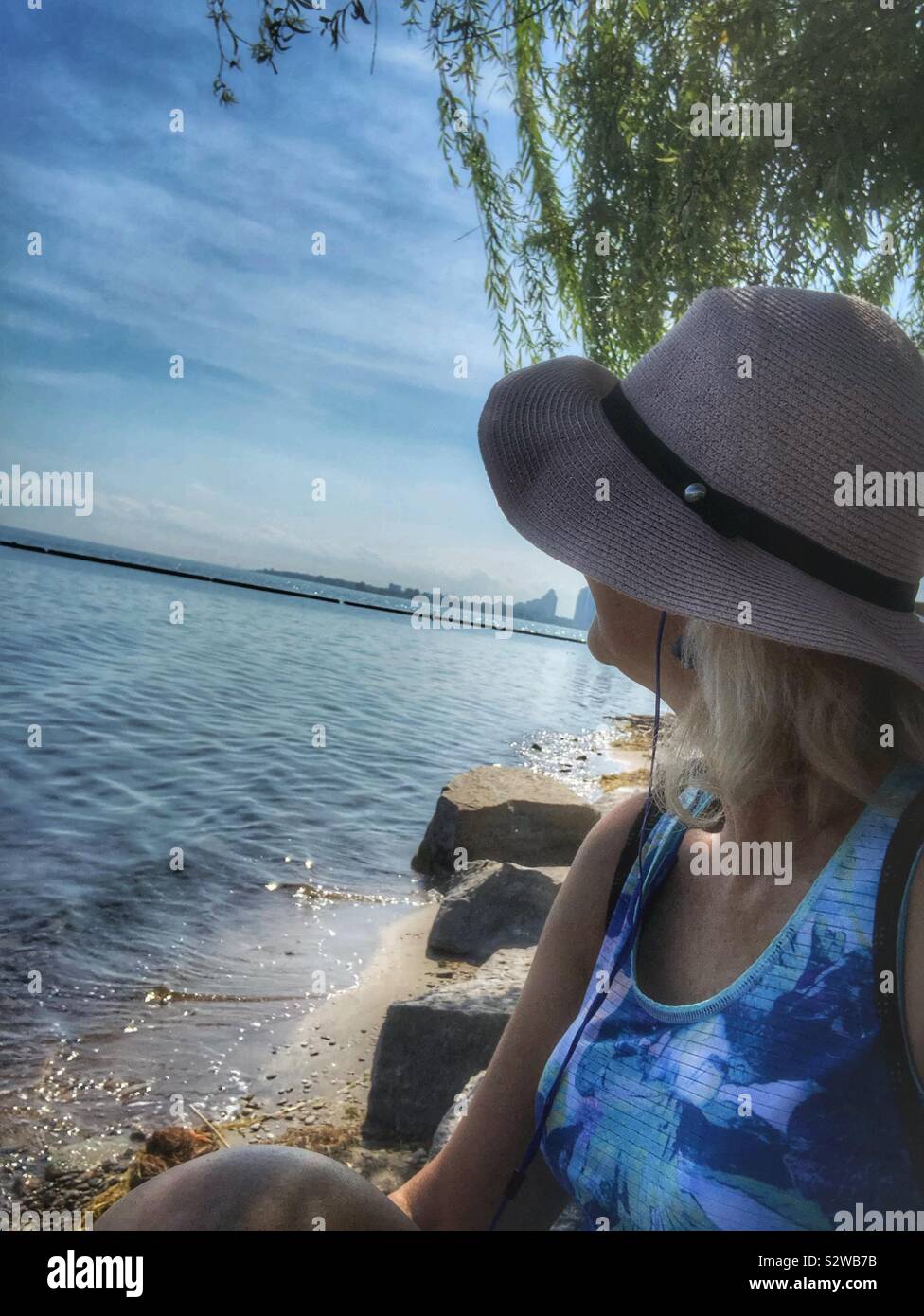 A woman sitting on rocks along the waterfront Stock Photo - Alamy