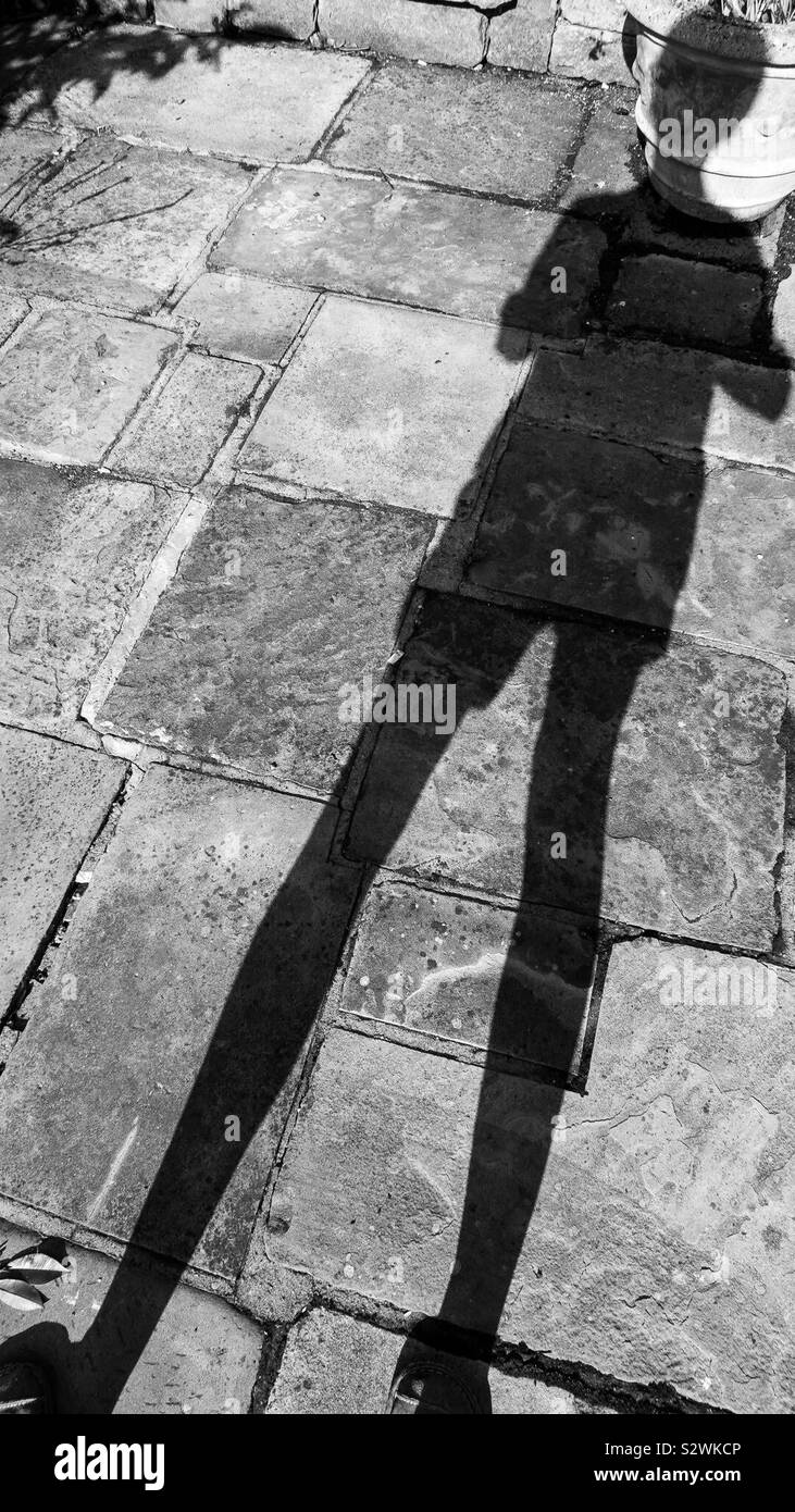 Shadow on a stone flagged path of a woman wearing shorts, black and ...