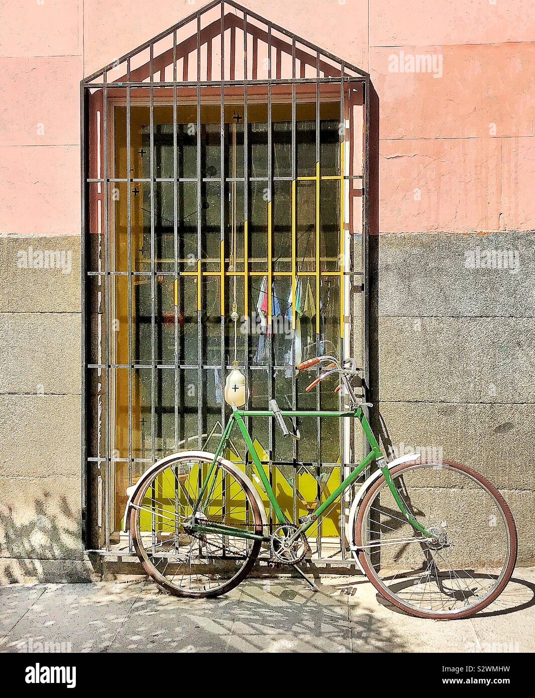 A bicycle is secured with a lock against a metal grill in front of a ...