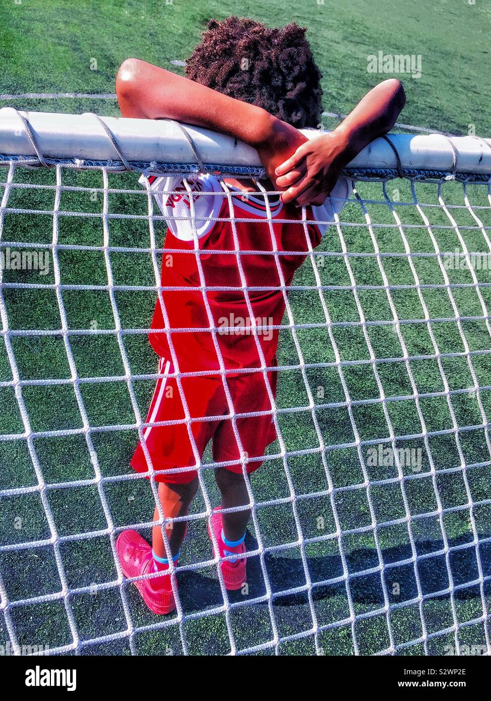 Boy in a red football strip leaning against the goal posts Stock Photo ...