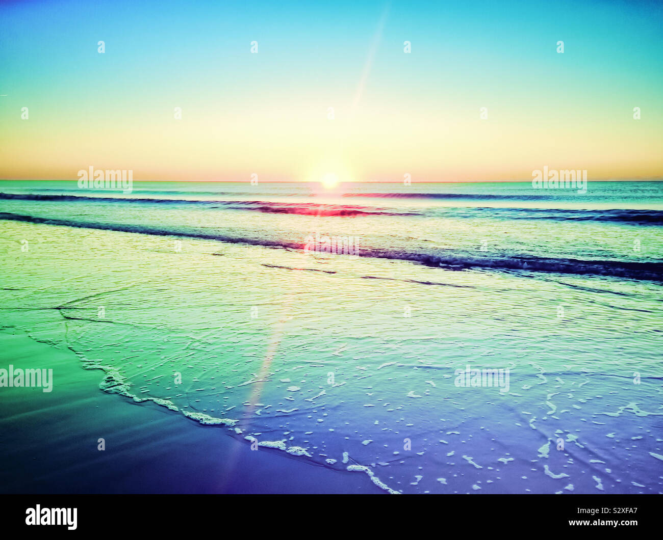 A vibrant colored sunrise with lens flare from the bright sun over the ...