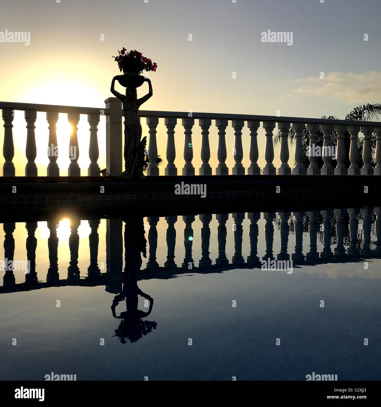 Symmetrical reflection of balustrades and statue in water at sunset ...