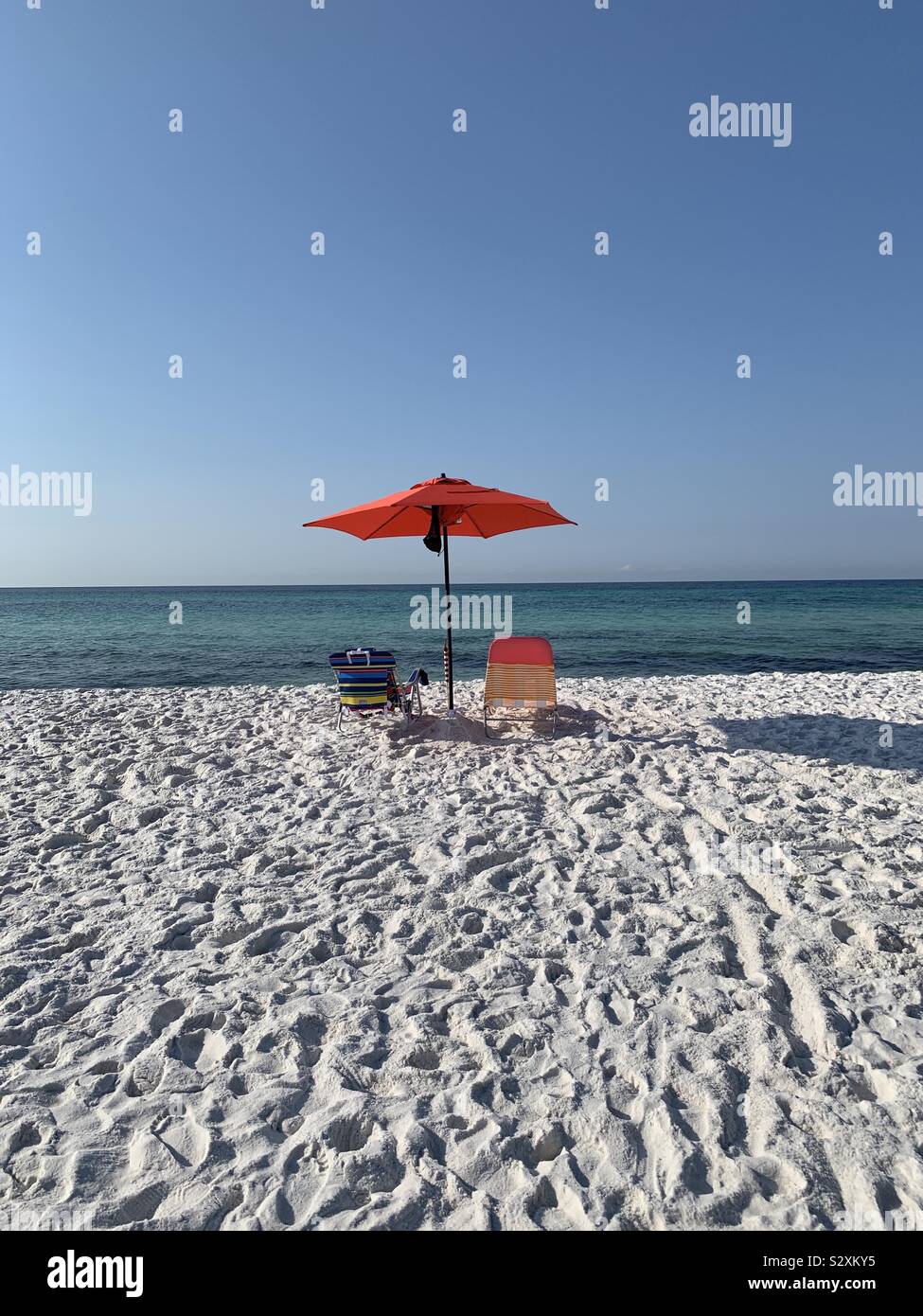 Two colorful beach chairs and umbrella from behind sitting on white ...