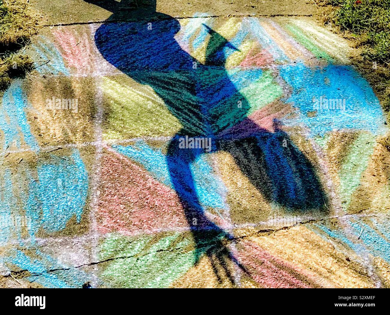 Girl’s dramatically posed shadow is cast across multicolored chalk ...