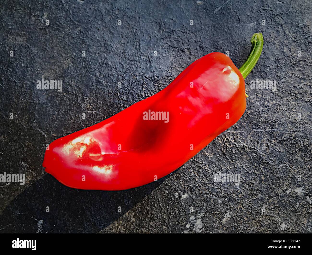 Single red pepper on a stone surface Stock Photo - Alamy