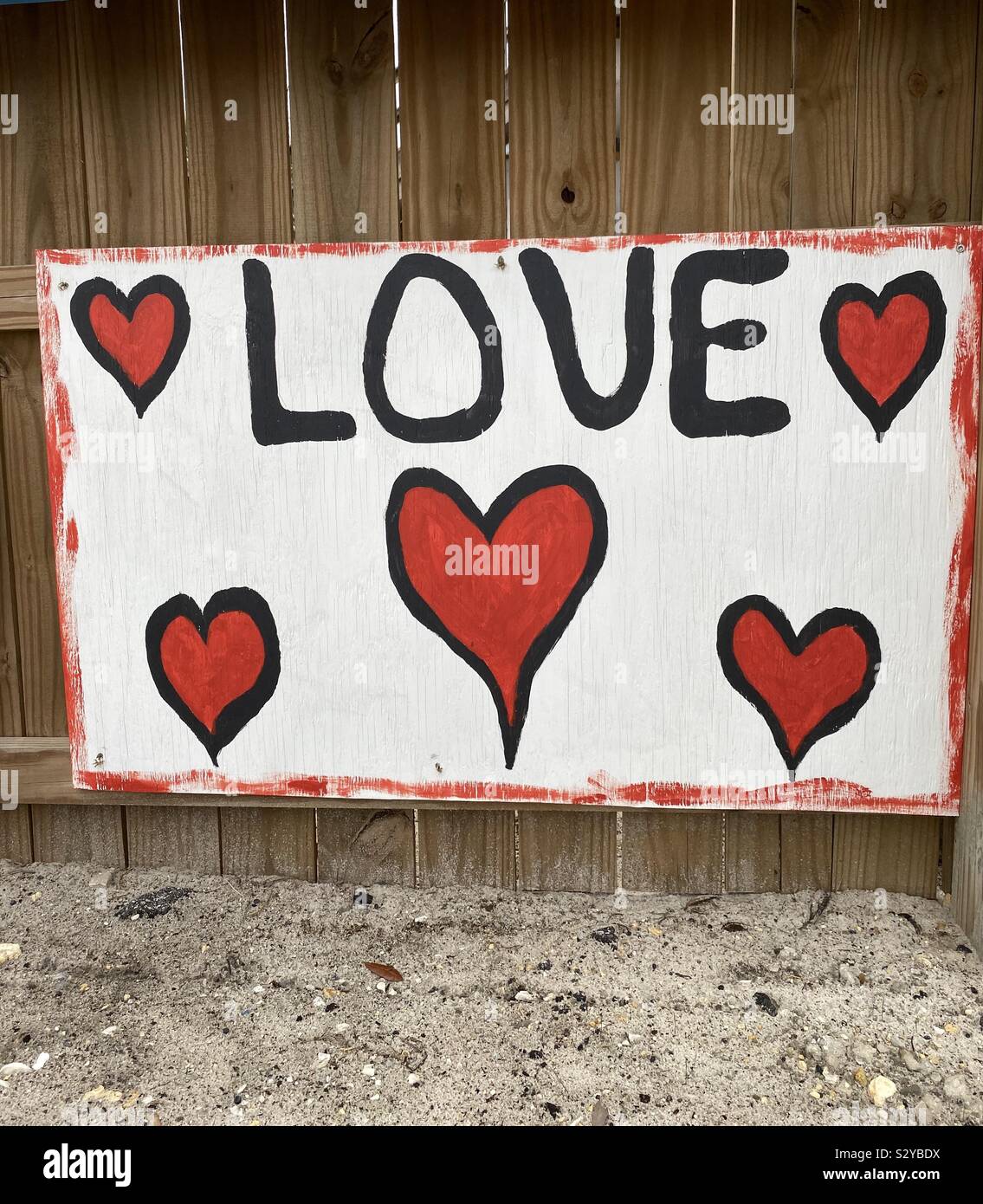 Outdoor painted sign hanging on a wooden wall that says love with ...