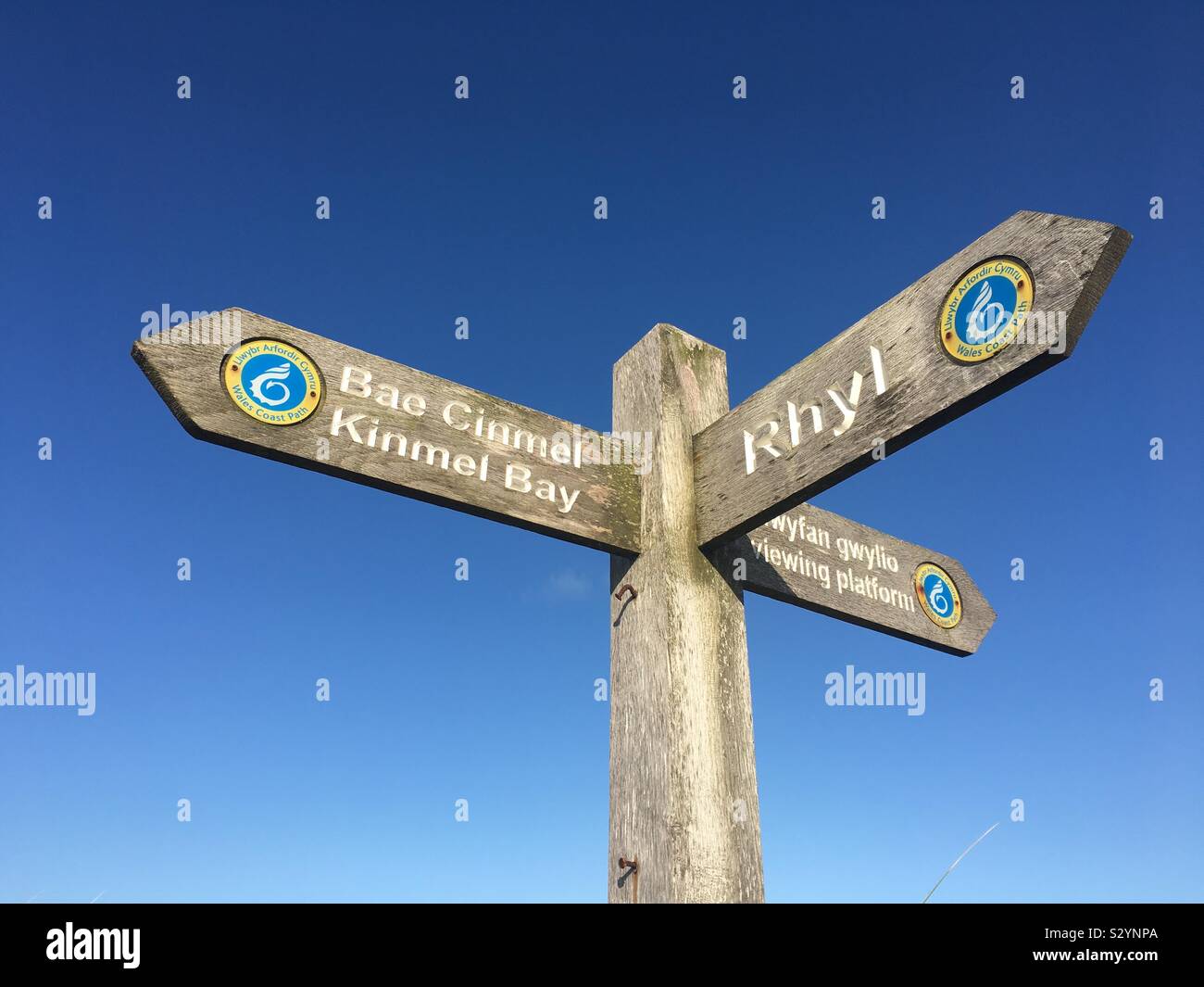 Three way wooden signpost, in North Wales, against a bright blue sky ...