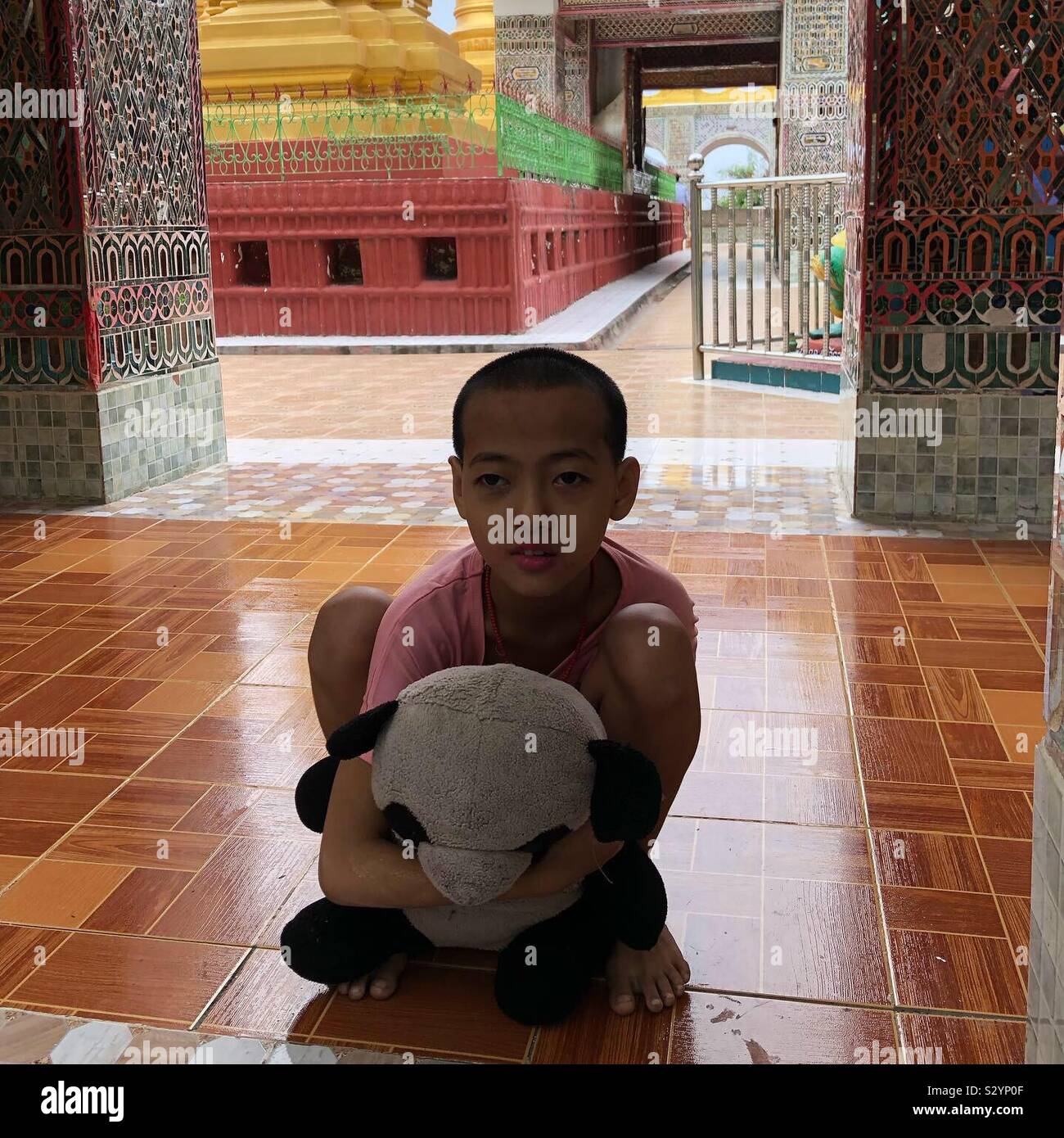 A young girl and her teddy bear sitting in a temple in Mandalay ...