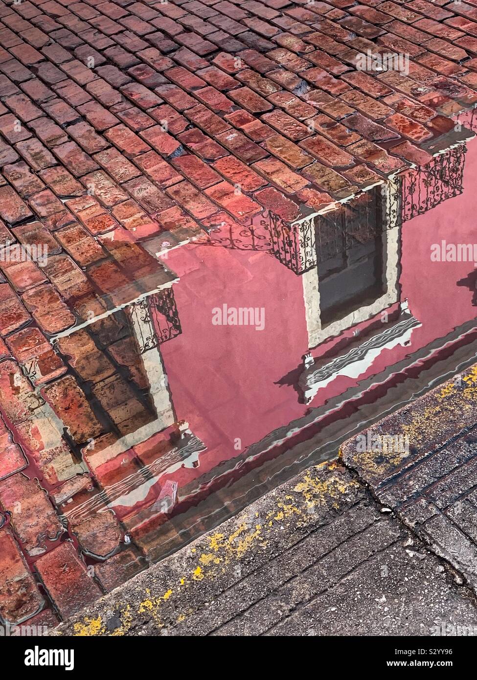 A pink building is beautifully reflected in a rain puddle curbside on a ...