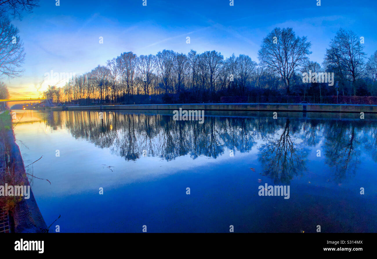 Deep blue winter sky with an early rising sun reflected in the water of ...
