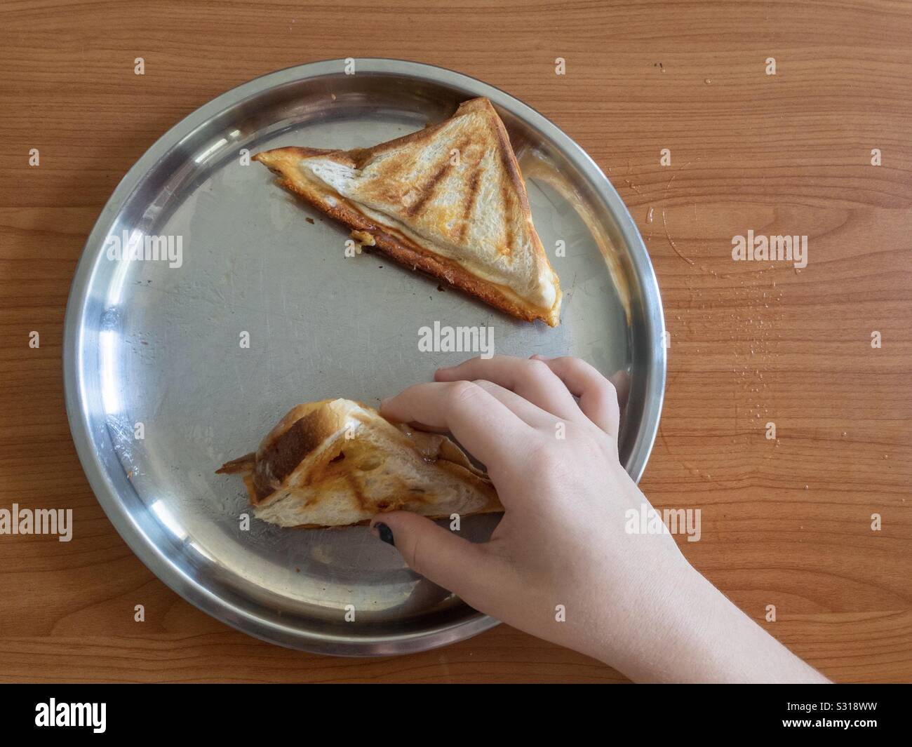 Hand of a young girl taking a toasted sandwich from a stainless steel ...