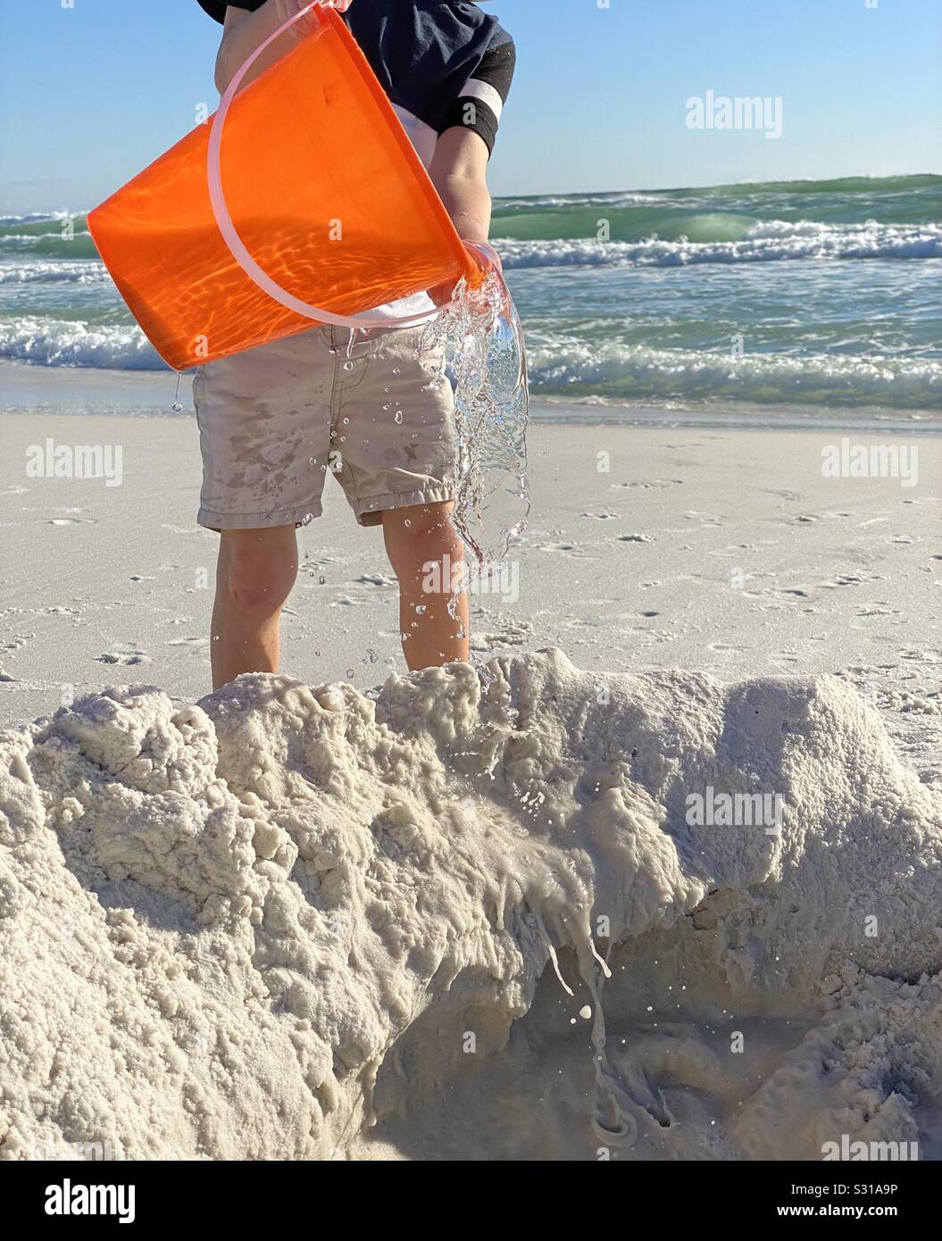 Little boy pouring a bucket of ocean water in a hole in the sand on the ...