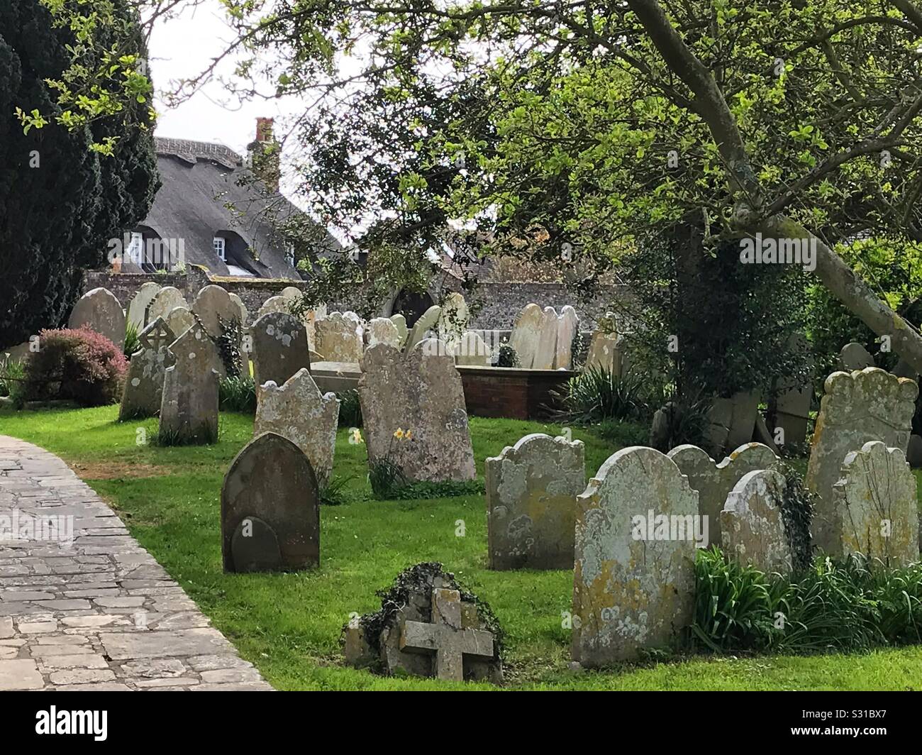 Country village churchyard with graves stones and thatched cottage ...