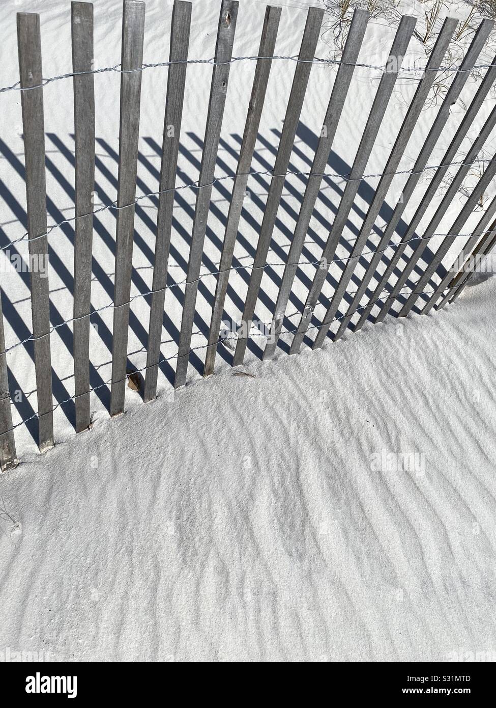 Abstract of a wooden fence on white sand beach with shadows of fence in ...