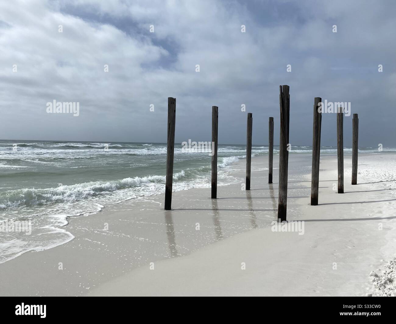 White sand beach in Destin, Florida with old wooden pier logs in sand ...