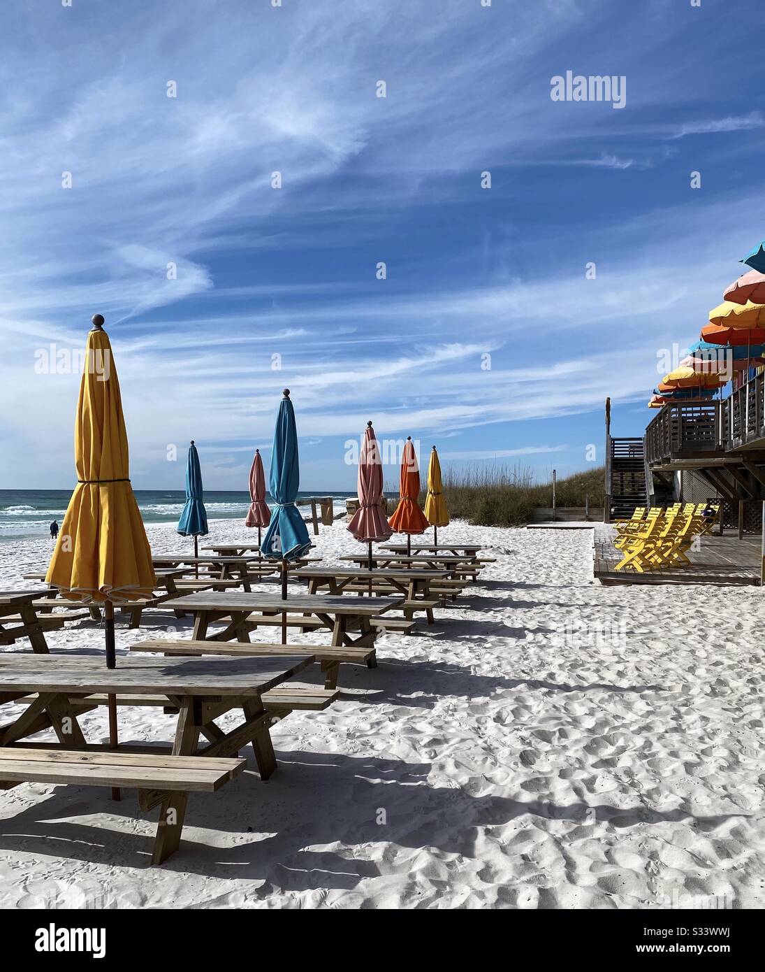 Outdoor picnic tables on white sand beach with colorful chairs and ...