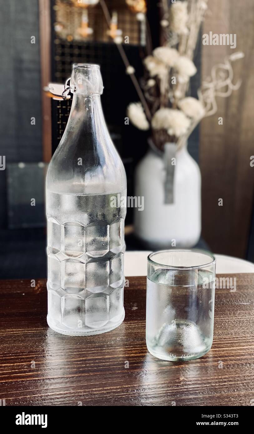 Simple glass bottle of water alongside a glass of water on a table with ...