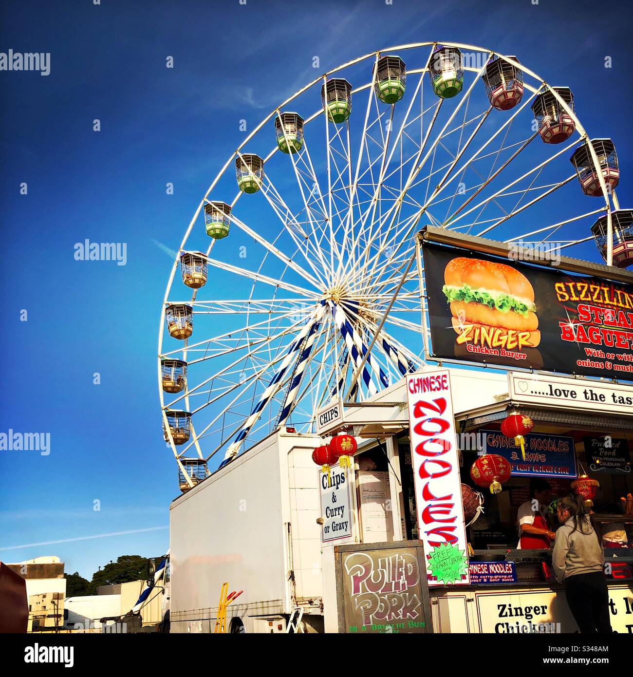 A tall Ferris wheel is seen behind a Chinese noodle food stall at a ...