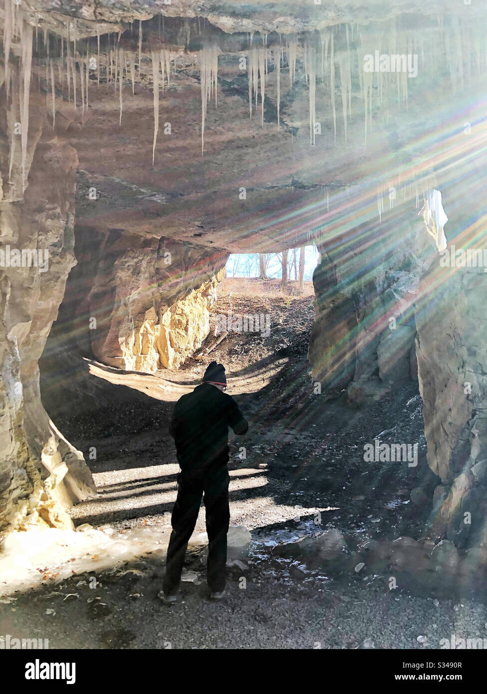 Man walking into cave with ice hanging from ceiling and rainbow lens ...