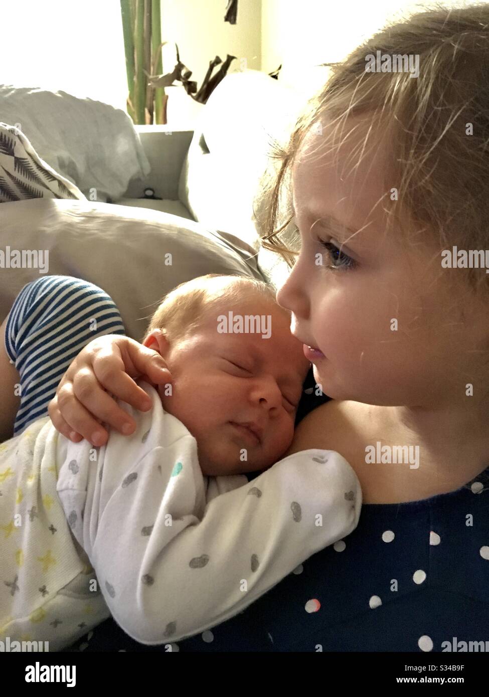 Four-year-old sister holding with her new baby brother Stock Photo - Alamy