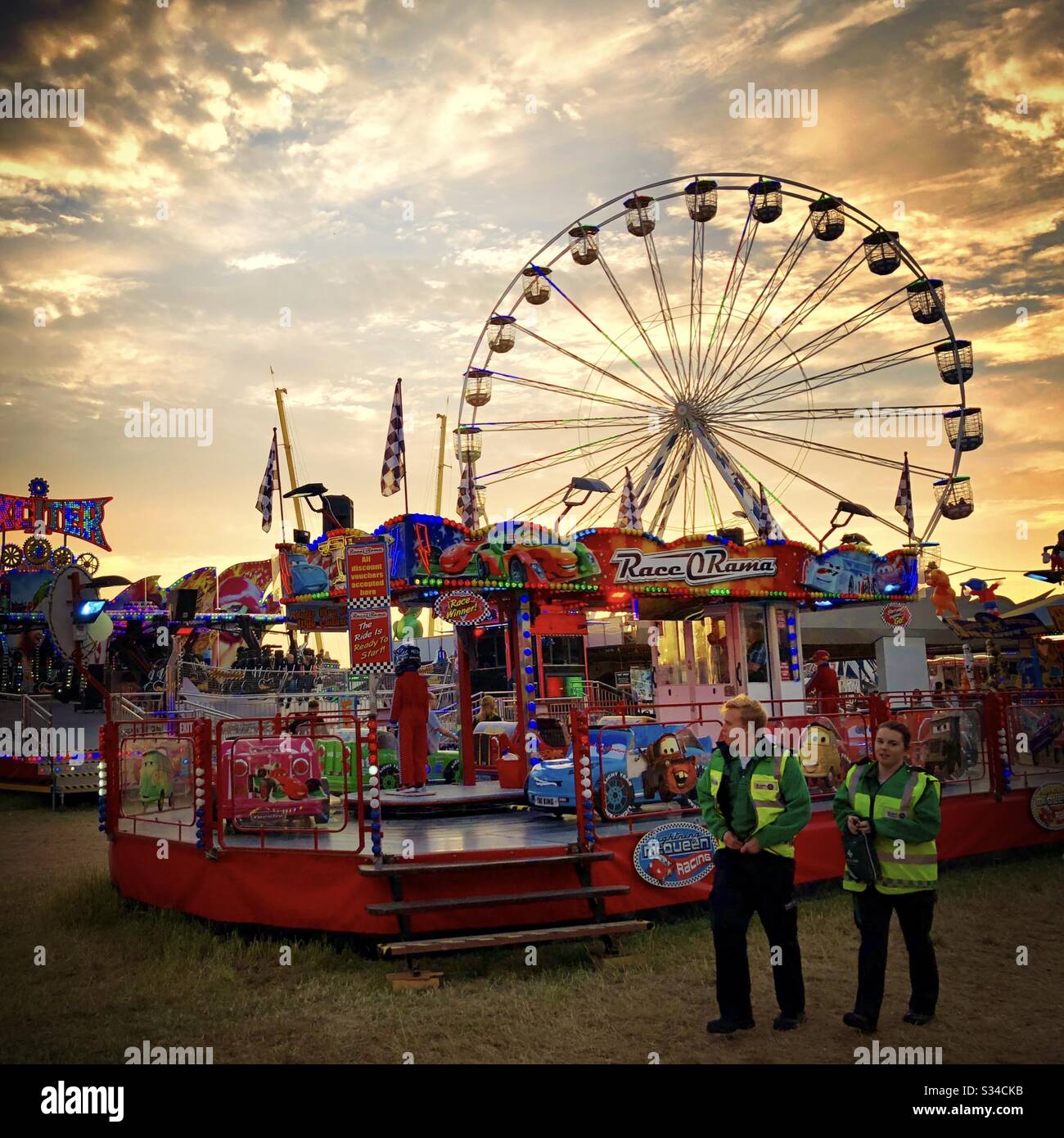 A backlit view of a Ferris wheel and dodgems ride during sunset at a ...