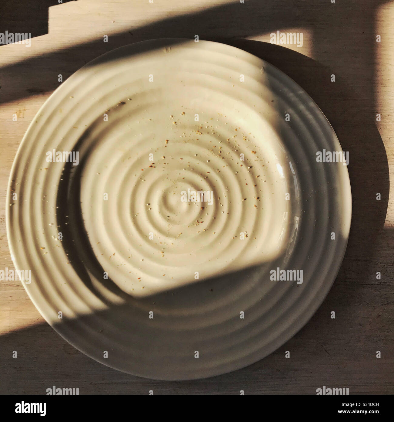 An empty plate with only crumbs on, caught in bright, shadowed light ...