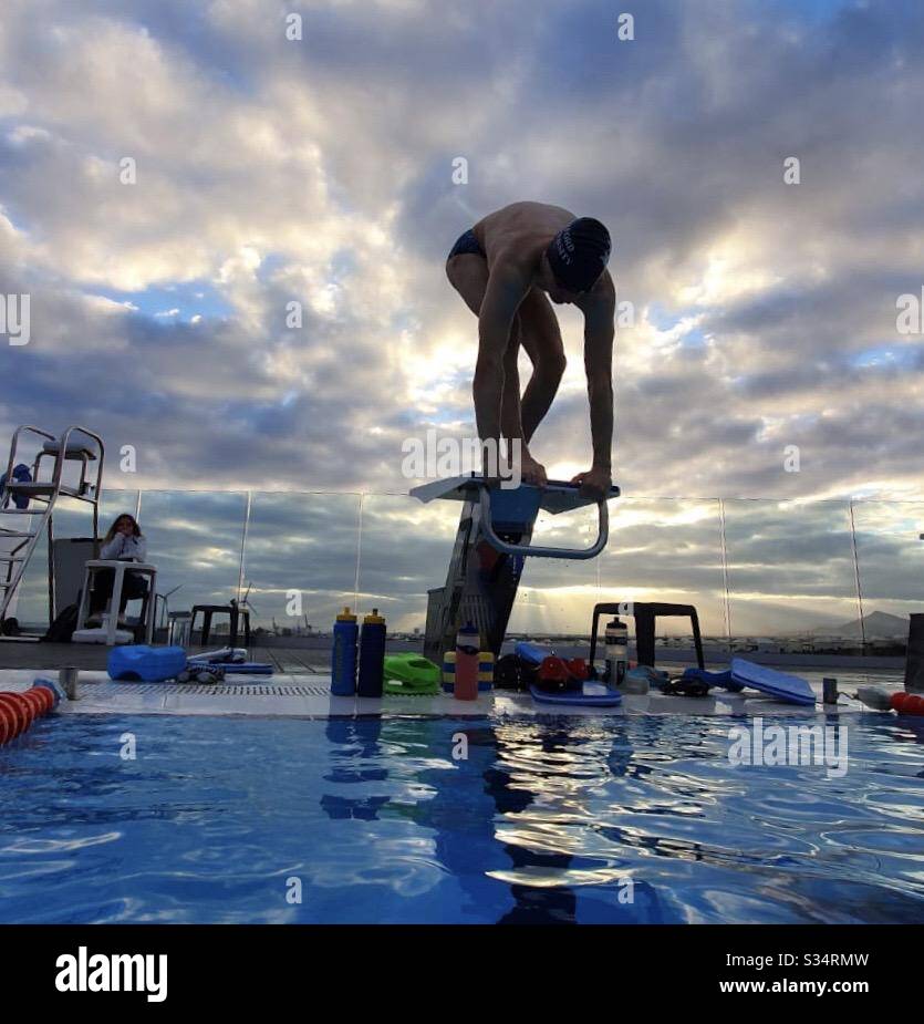 Swimmer on block about to dive into swimming pool at sunset Stock Photo ...
