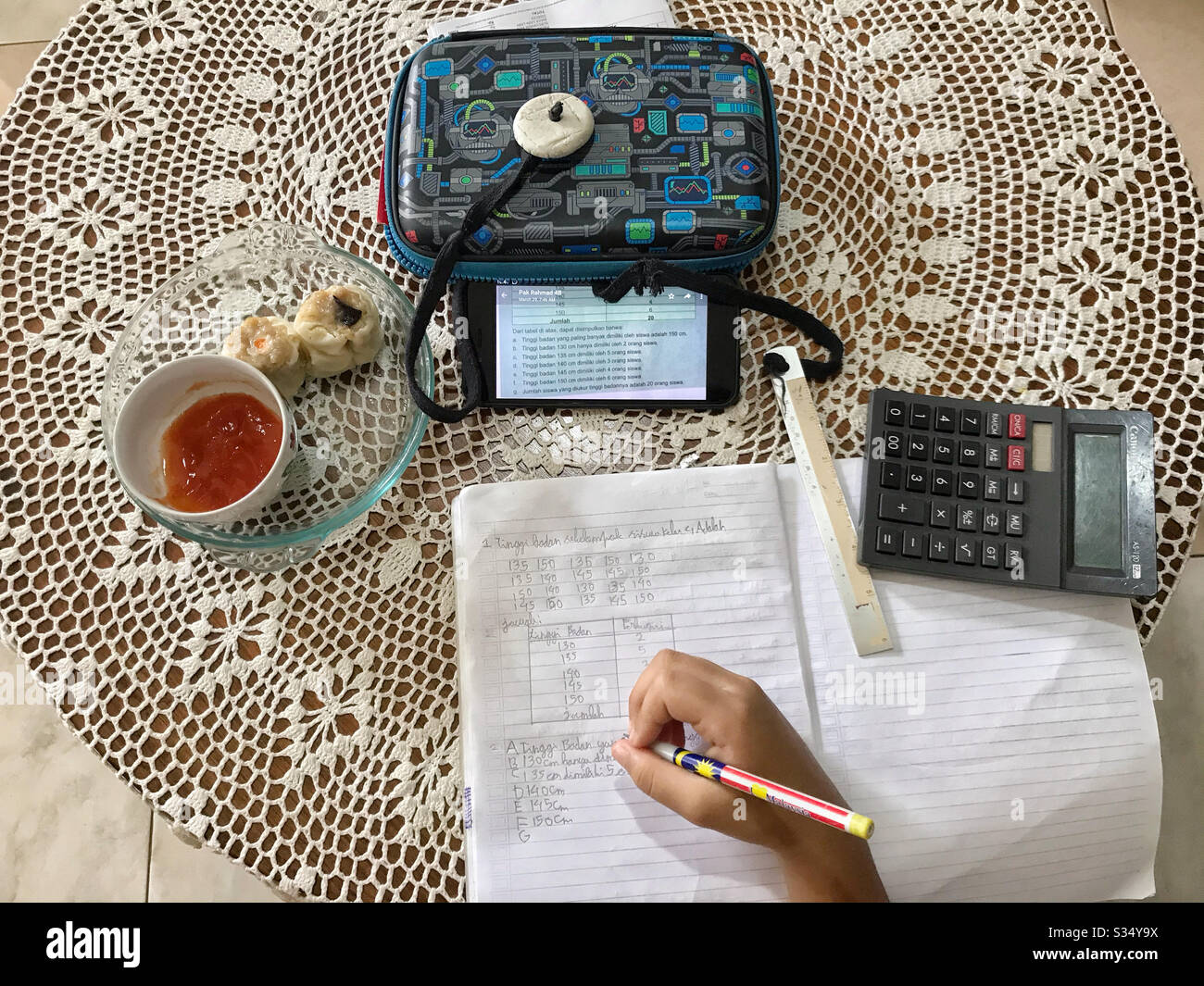 A kid write down the homework that appears on the smartphone screen ...