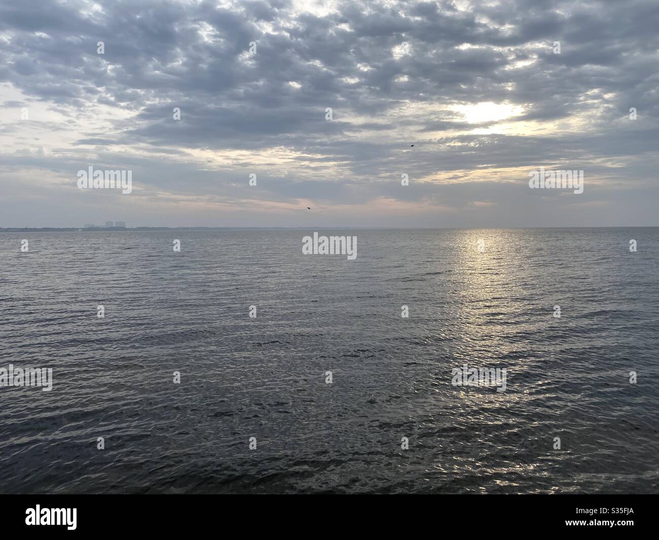 Soft sunset skies over bay water with sun reflections on water and ...