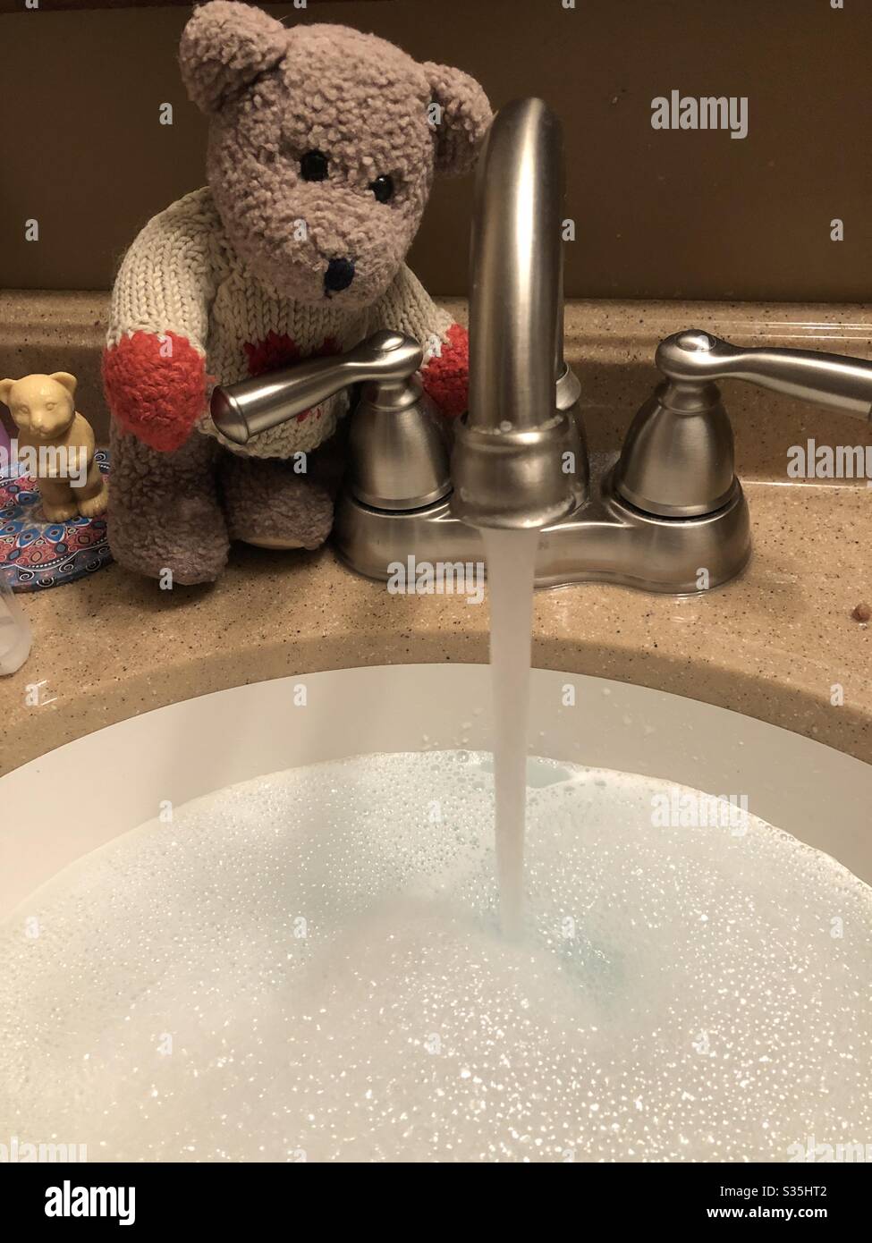 A small teddy bear turning on the tap filling the sink for his bath ...