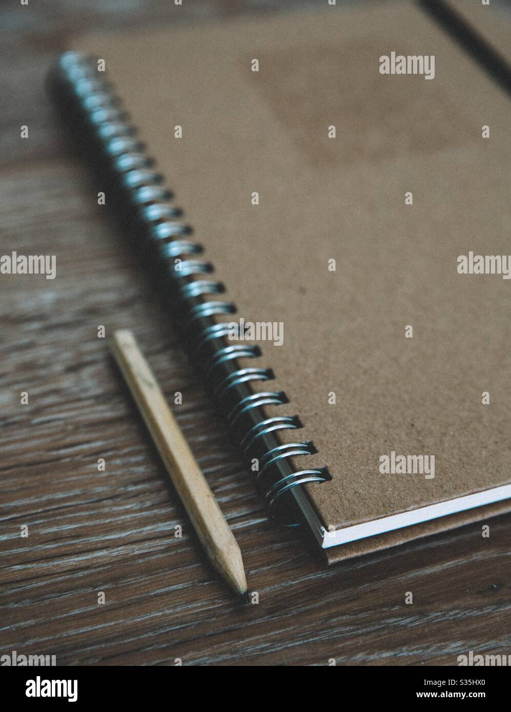 An old fashioned spiral notebook with pencil on a wooden desk top with ...