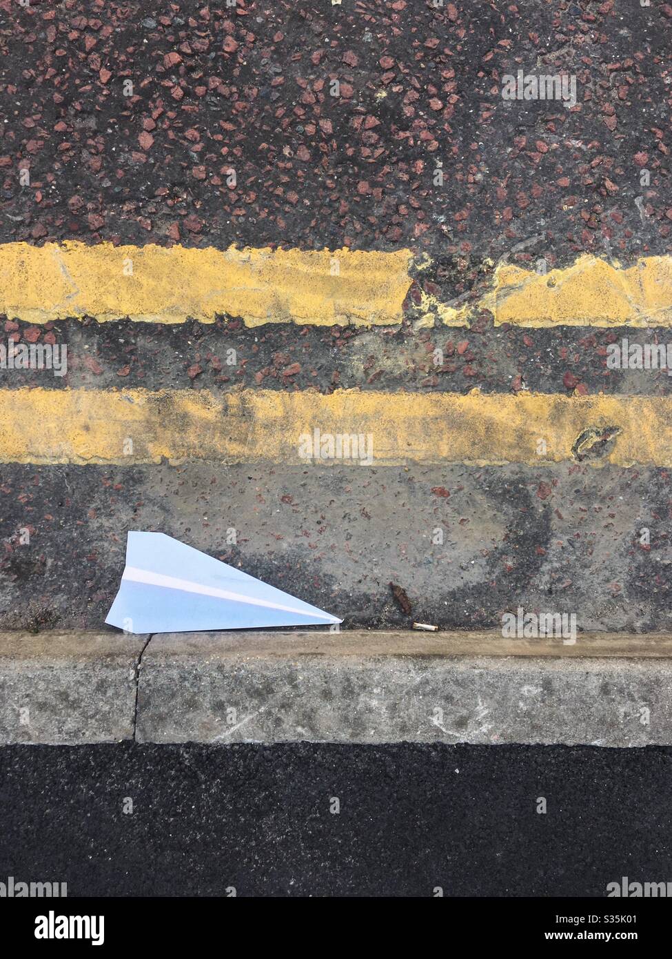 A paper airplane in a gutter by double yellow lines Stock Photo - Alamy