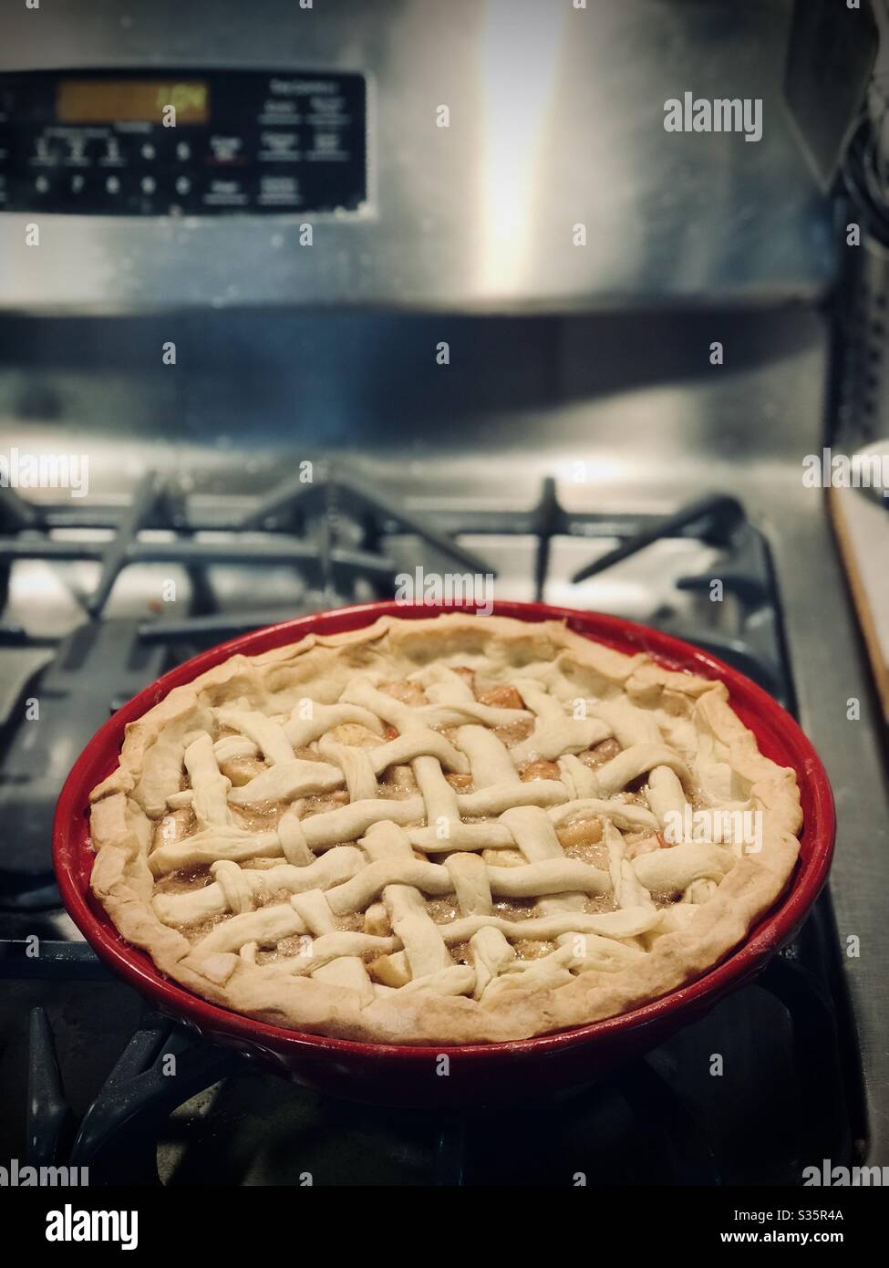 A latticed top apple pie in a red dish on top of a silver stove top ...