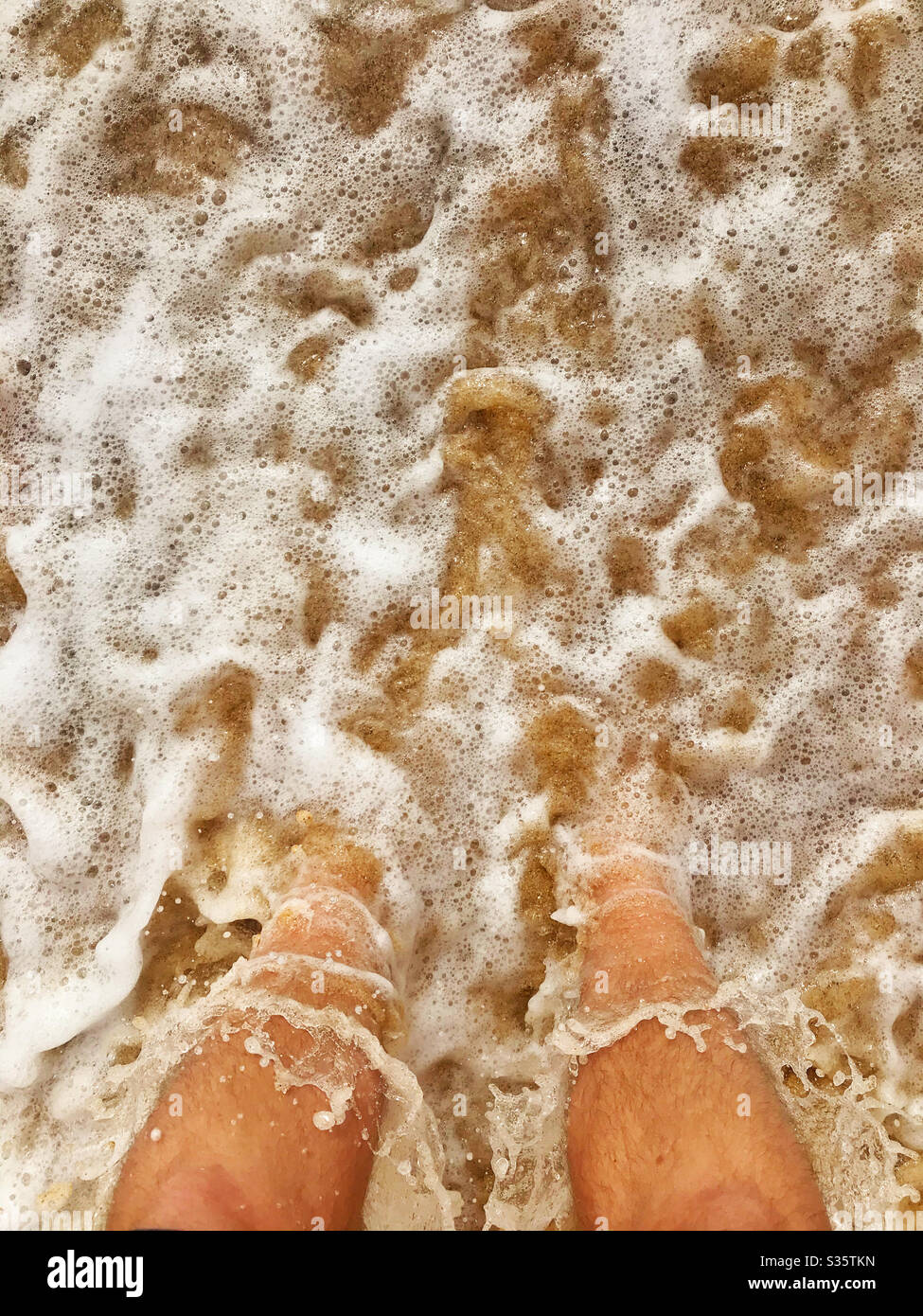 A pair of feet on a beach being submerged by a wave Stock Photo - Alamy