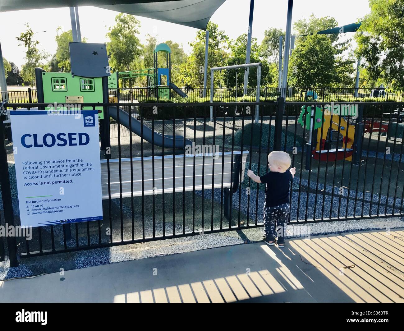 A young child standing by a ‘closed’ sign at a playground due to ...