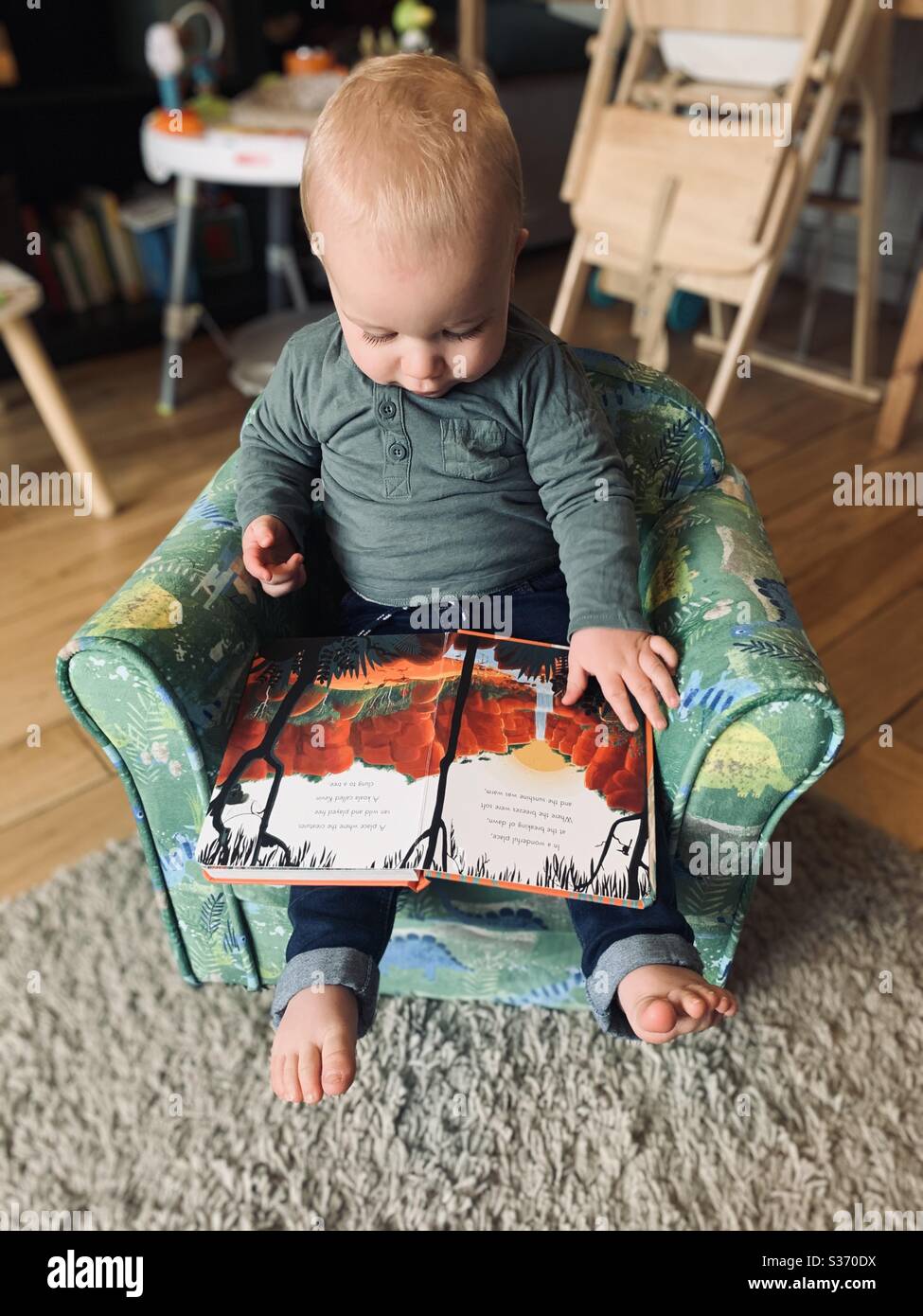 Toddler reading book in chair Stock Photo - Alamy