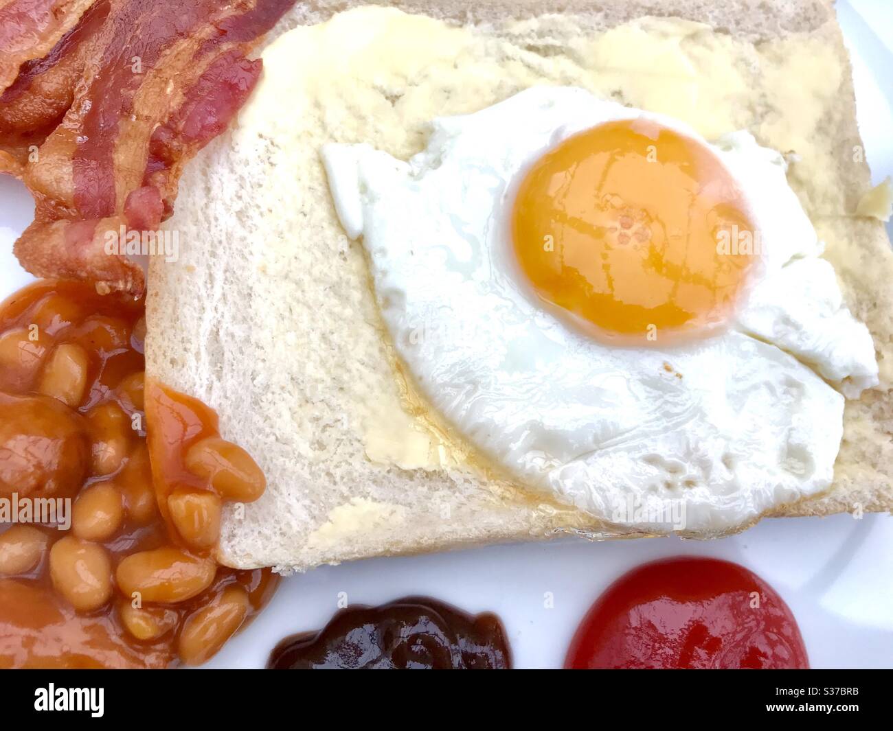Fried egg on buttered white bread with bacon and baked beans Stock ...