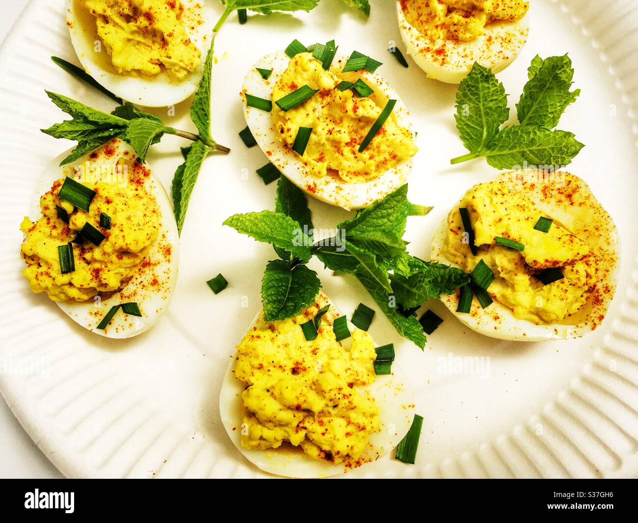 Devilled eggs with garlic chives and sprigs of mint on paper plate ...