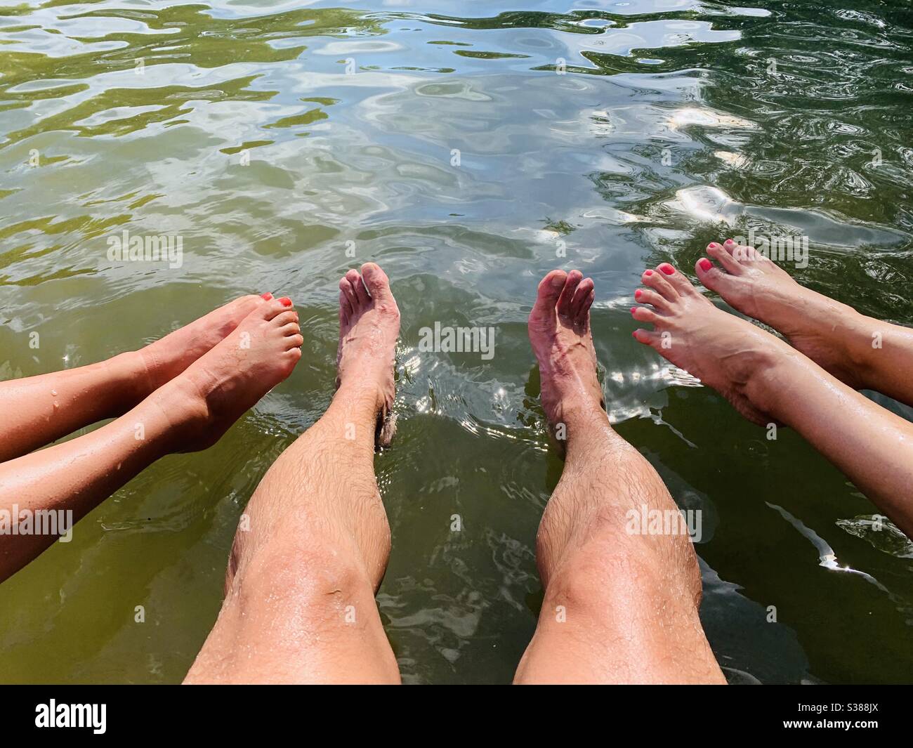 Three sets of legs dipping feet in water Stock Photo - Alamy
