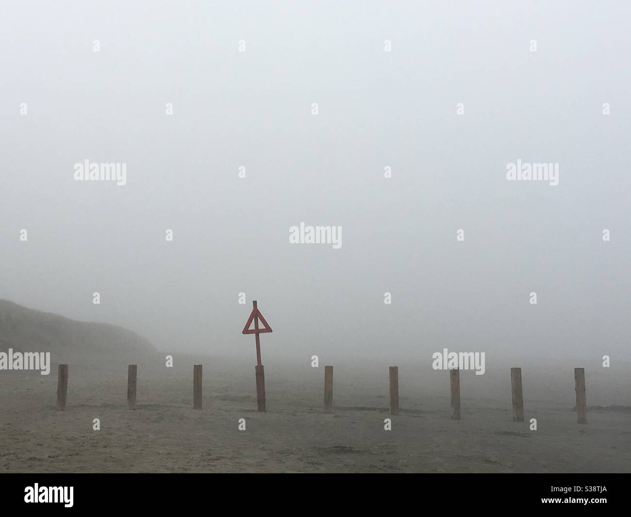 Misty beach with wooden pillars and triangular warning sign Stock Photo ...