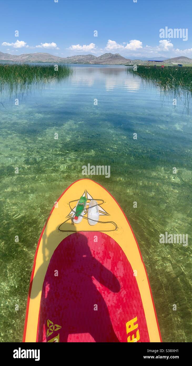 Shadow of woman on paddle board with clear water and mountains in ...