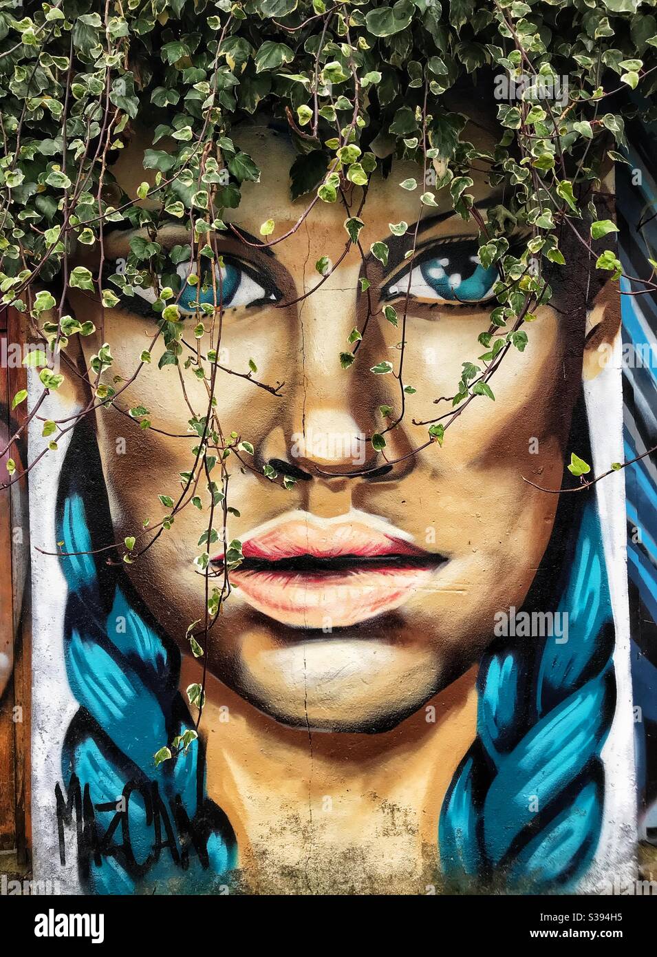 Graffiti painted wall of ladies face with real leaves and foliage ...