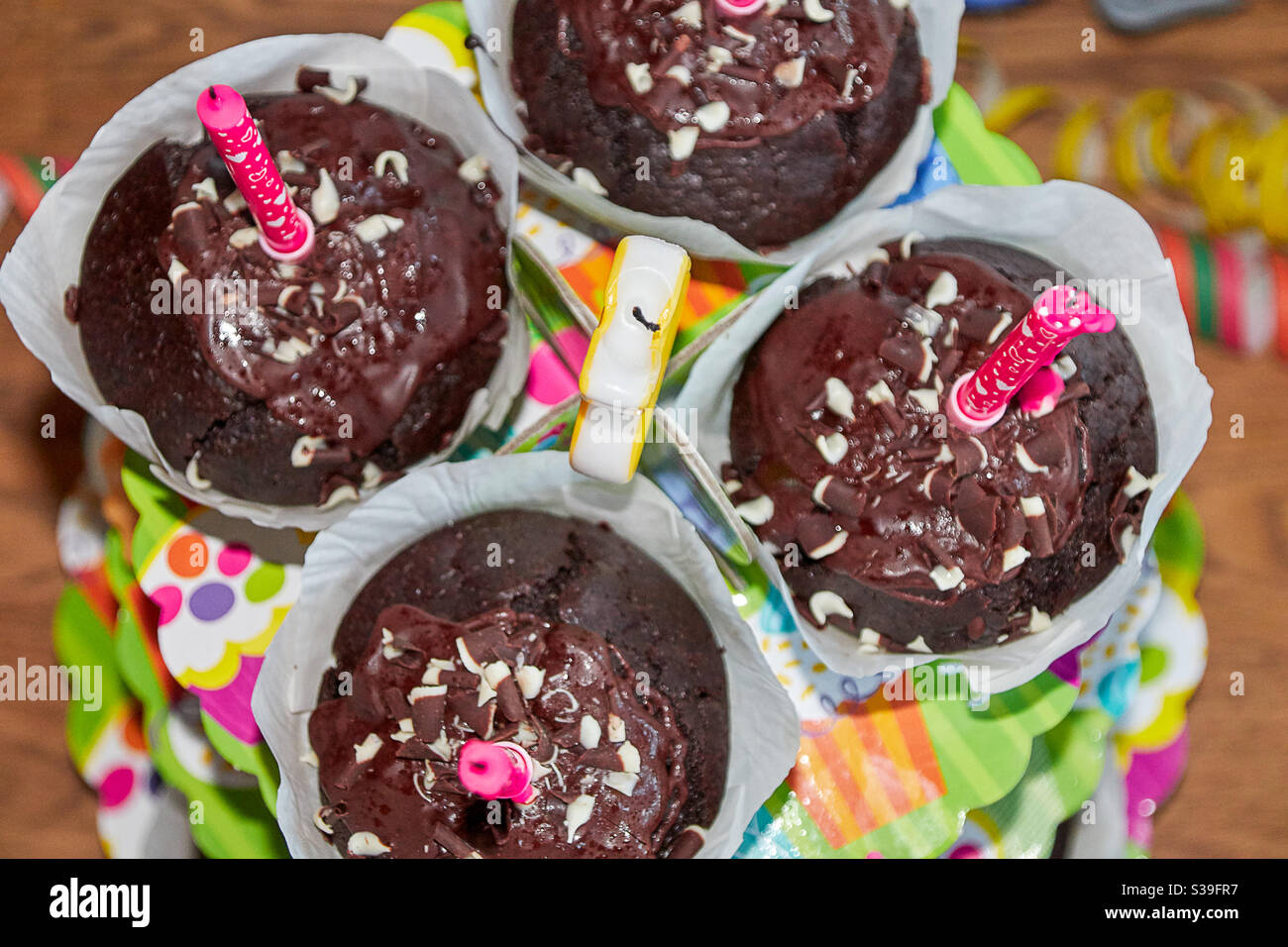 four birthday chocolate muffins with candles and colorful decoration on ...