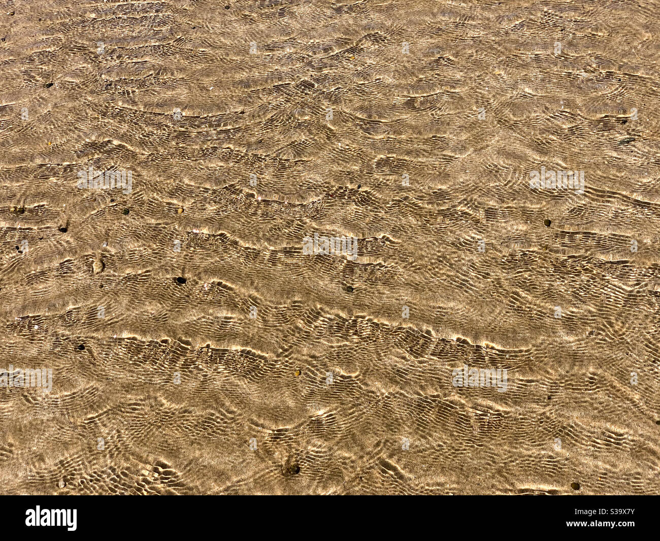 Shallow water washing over the sand making patterns with the sunlight ...
