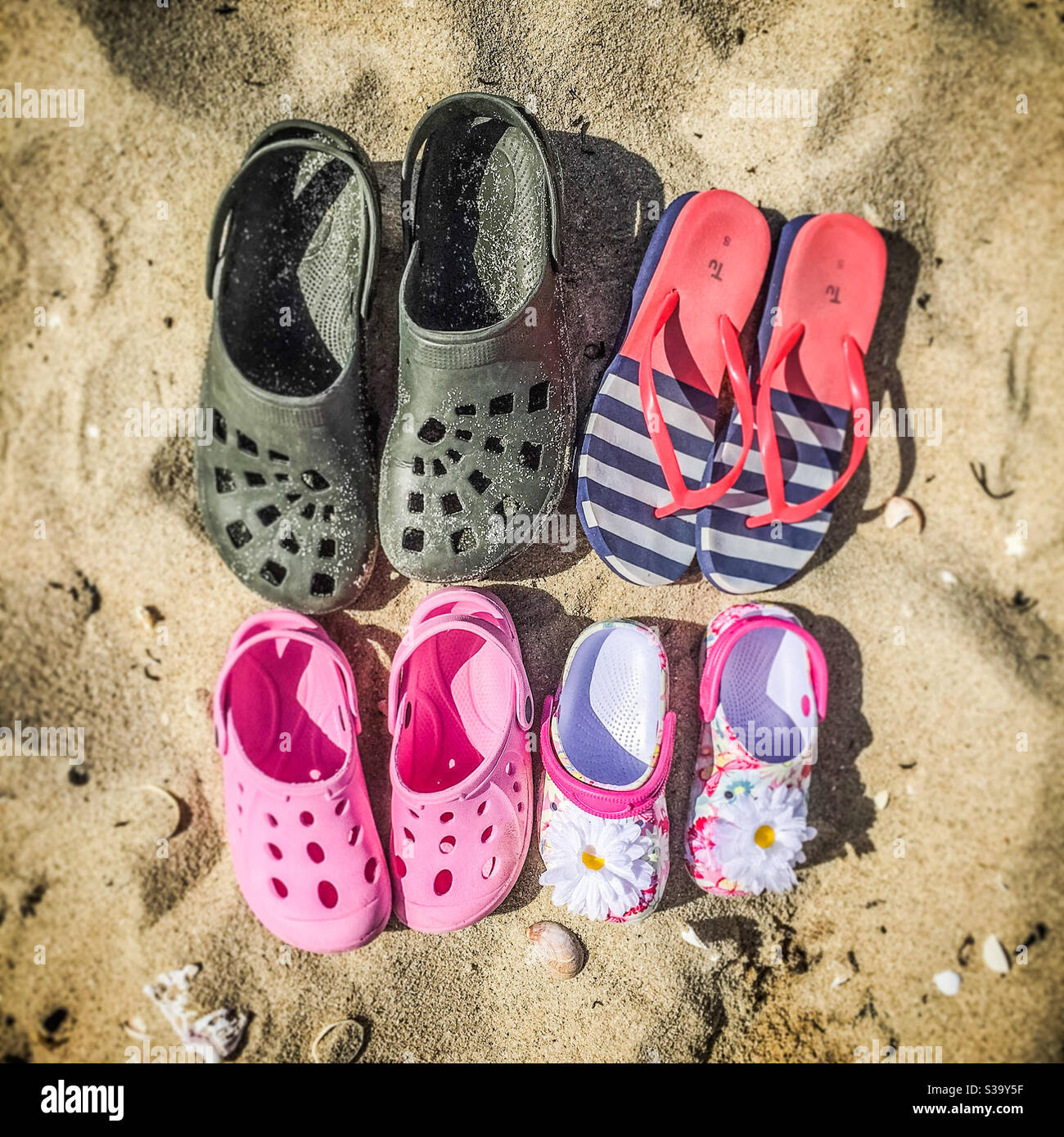 Four pairs of crocs and flip flops on a sandy beach Stock Photo - Alamy