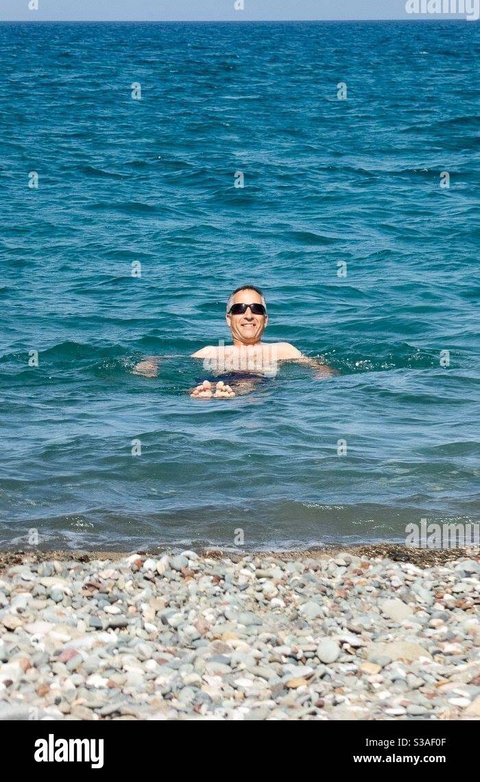 Man floating in deep blue sea, pebble beach, blue sky Stock Photo - Alamy